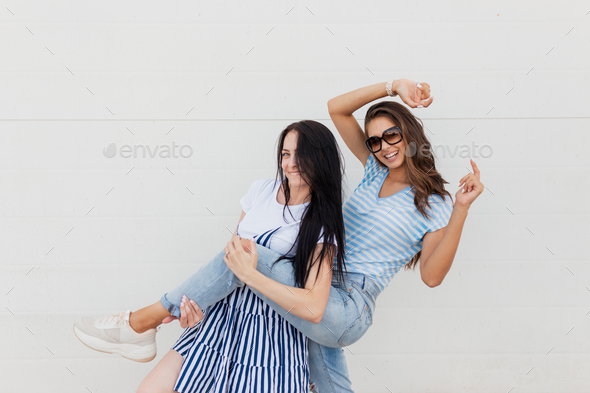 Two Young Slim Dark Haired Ladies Wearing Casual Outfit Stand Next To