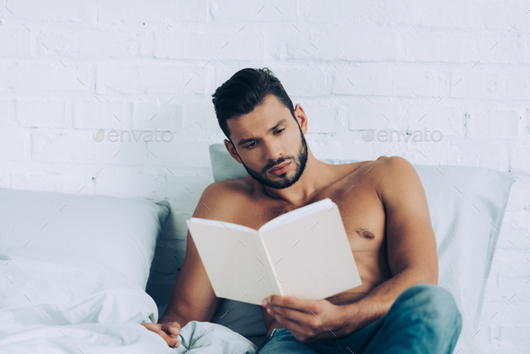 shirtless muscular man reading book during morning time in bedroom at ...