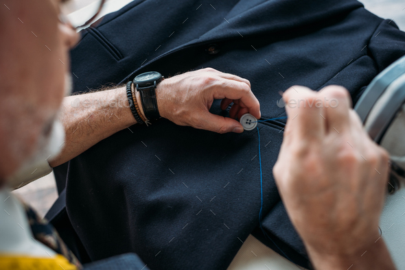 cropped image of tailor sewing button to jacket at sewing workshop ...