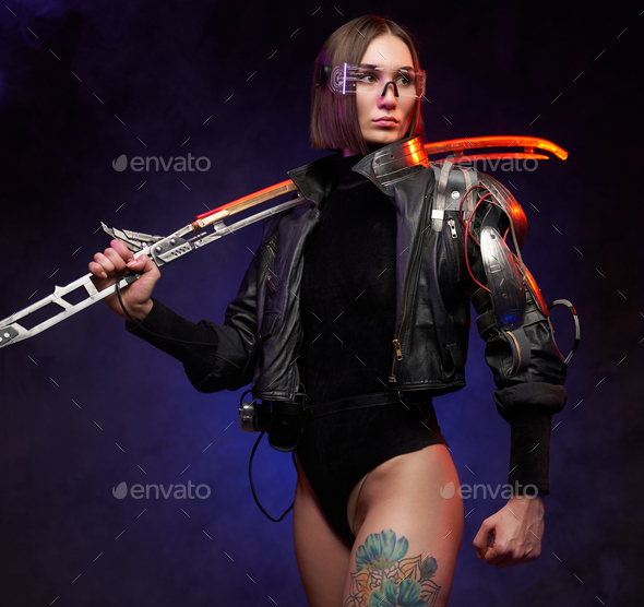 Urban and cyberpunk styled woman assassin with sword posing in studio ...