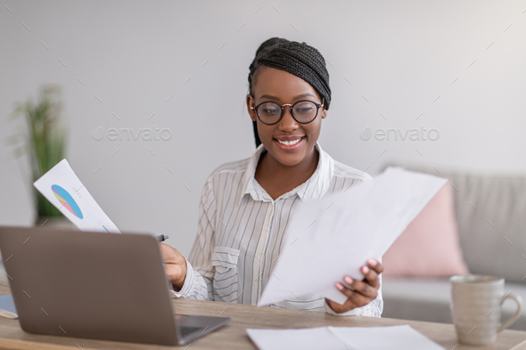 Smiling black woman financial manager working with papers from home ...