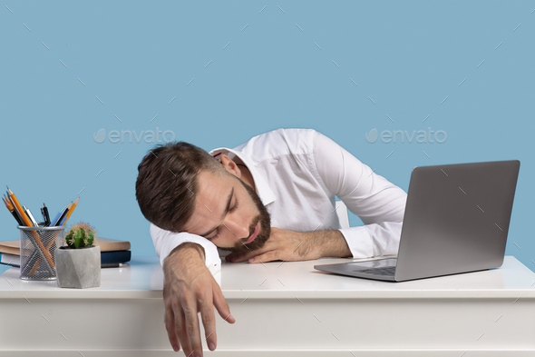 Exhausted young businessman sleeping on his desk, tired of overworking ...