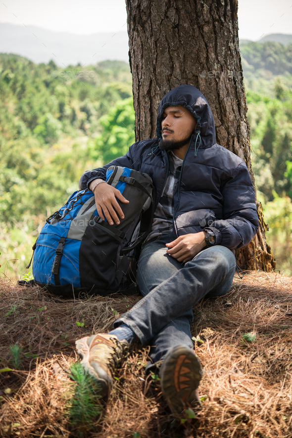 Portrait of young beard man sitting alone by a tree with backpack ...