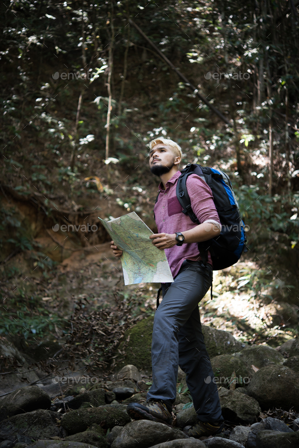Adventure man observing map on a mountain path to find the the right ...