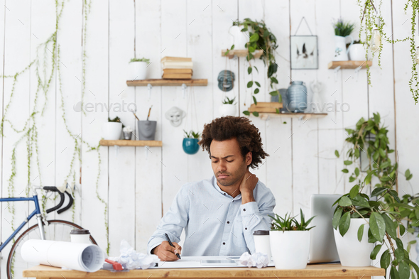 Overwork concept. Tired sleepy engineer rubbing his neck after working ...