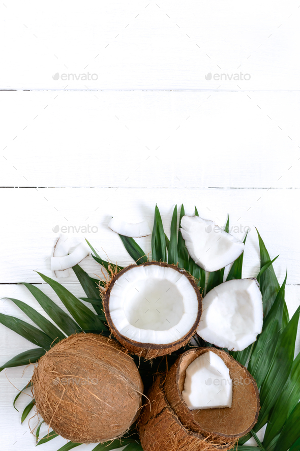 Whole coconut, shell and green leaves on a white wooden background ...