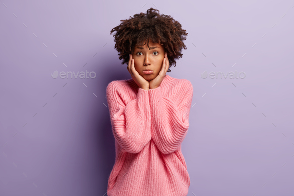 Sad dejected African American woman touches cheeks with both hands, has ...