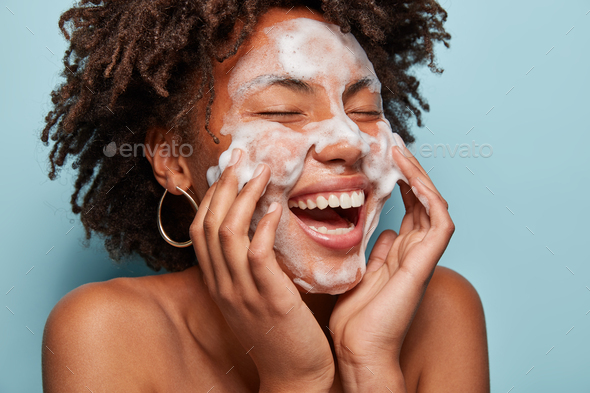 Cheerful black female model applies foaming cleanser, has clean fresh ...