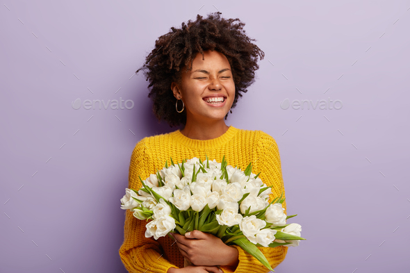 Satisfied dark skinned lady with overjoyed facial expression, closes ...