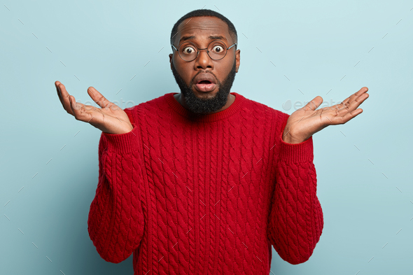 Ethnic hesitant man has surprised clueless expression, spreads hands ...