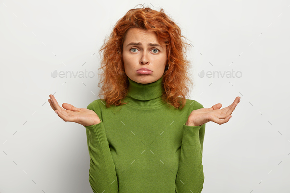 Hesitation and confusion. Sad displeased redhaired woman shrugs ...