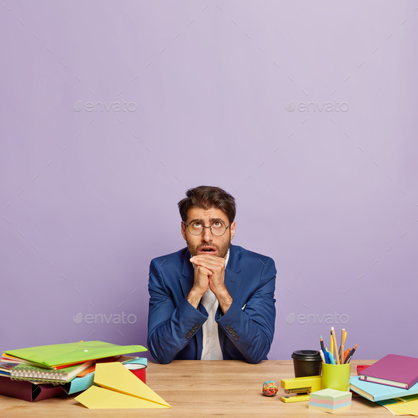 Worried young male manager believes in better, keeps hands together and ...