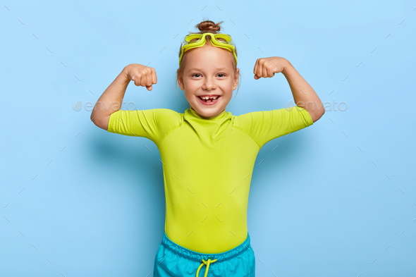 Positive little girl spends leisure time in water park, raises arms and ...