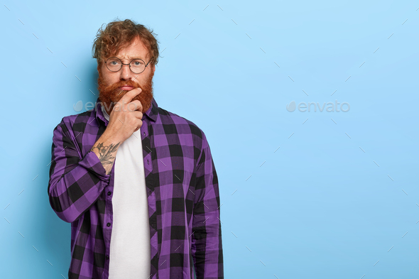 Serious pensive man scowls eyebrows and touches chin, being deep in ...