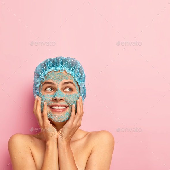 Happy satisfied woman touches both cheeks with hands, wears blue facial ...
