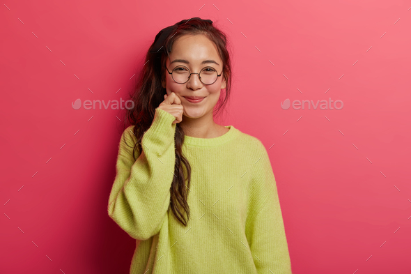 Pretty cheerful girl with dark hair, keeps hand on cheek, has pleased ...