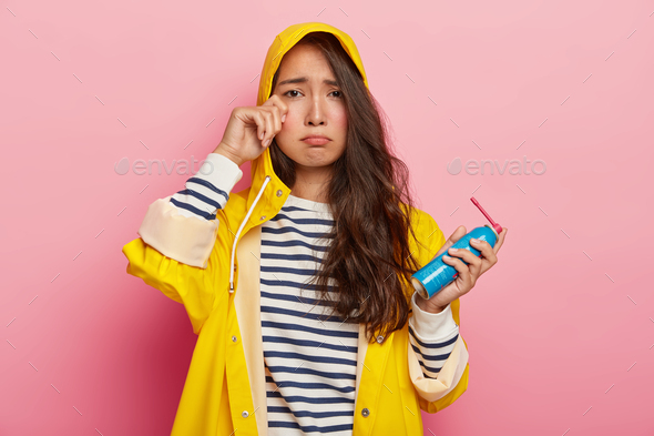 Dejected Asian woman cries from despair, rubs eye holds bottle of spray ...