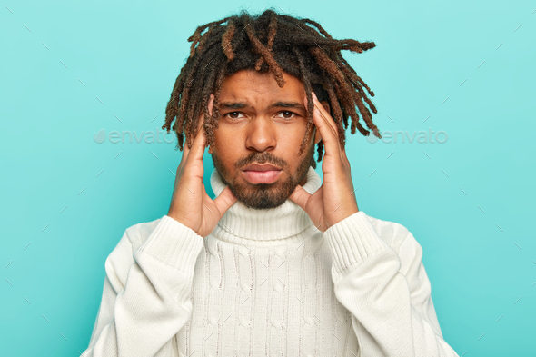 Portrait of unhappy dark skinned man with dreads, suffers from ...