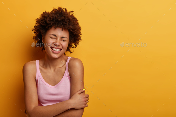 Cheerful overjoyed woman crosses hands over chest, laughs out loudly ...