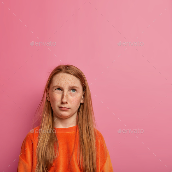 Photo of pensive ginger girl looks thoughtfully above, smirks face and ...