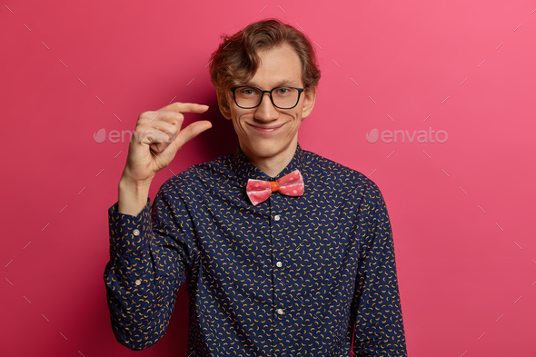 Handsome positive nerd man does small size hand sign with fingers ...