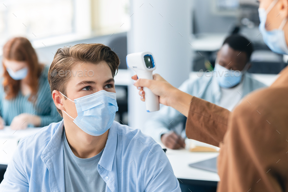 Teacher with contactless thermometer measuring temperature of student ...