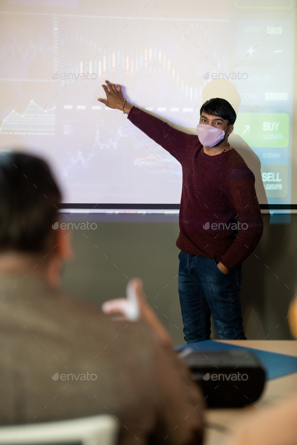 Young confident business coach pointing at one of several graphs on ...