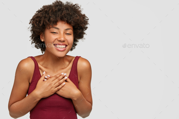 Touched moved pleased dark skinned girl keeps both palms on chest ...