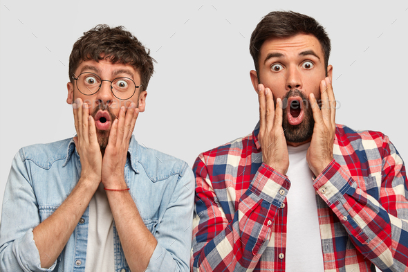 Two young bearded scared men stare at camera, touch cheeks, being ...