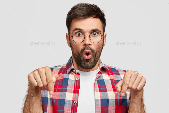 Surprised guy with stunned expression points down, has eyes popped out ...