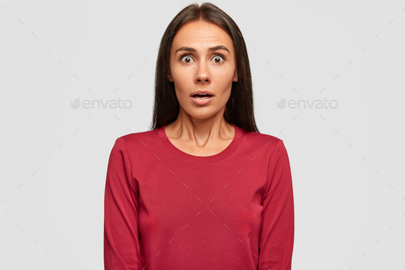 Stupefied brunette young woman stares with bugged eyes, opens mouth ...