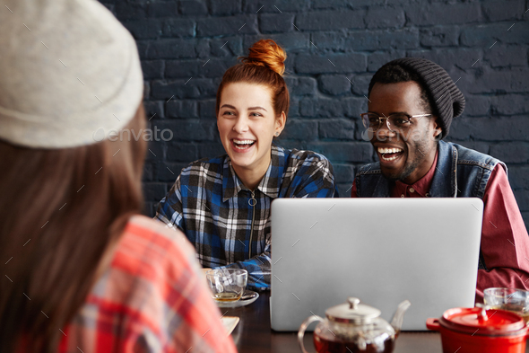 Three happy enthusiastic young people using laptop computer, chatting ...