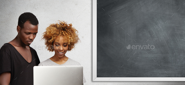 Two African college students using laptop in classroom. African girl ...