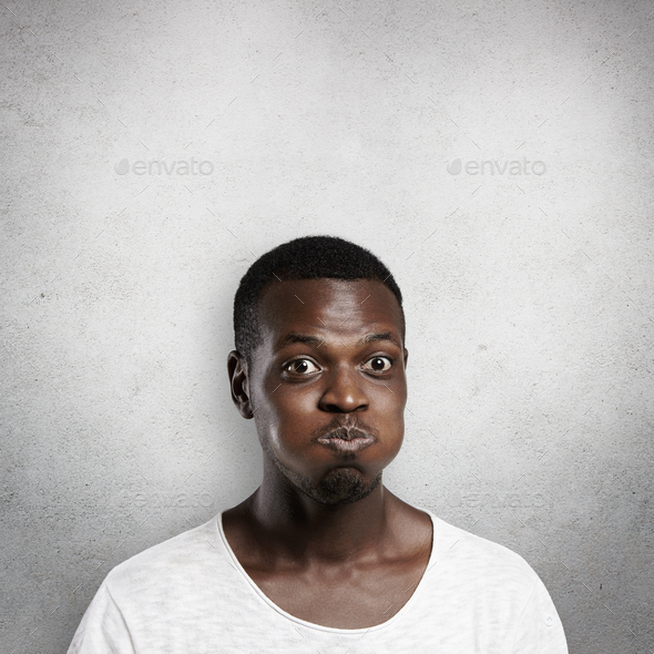 Body language concept. Young dark-skinned man puffing cheeks, trying ...