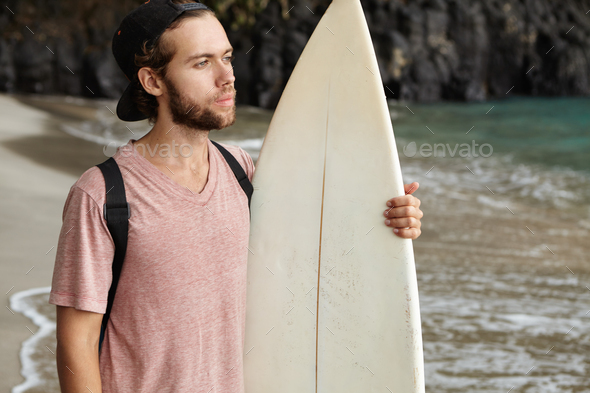 Outdoor shot of attractive bearded surfer holding his white surfboard ...