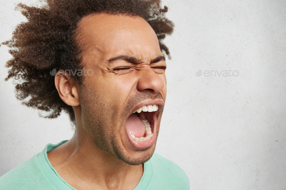 Close up portrait of mad angry young dark skinned male screams in anger ...