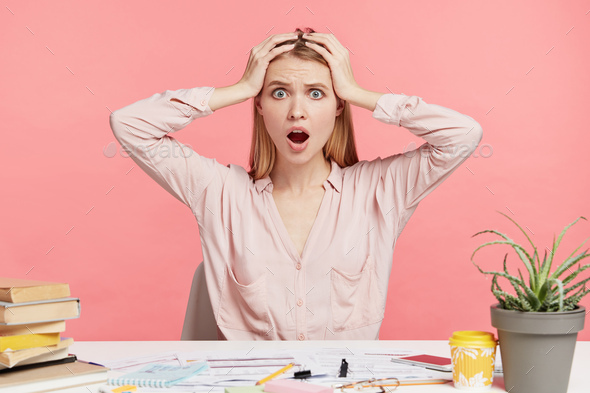 Shocked stupefied beautiful woman dressed in blouse, keeps hand on head ...