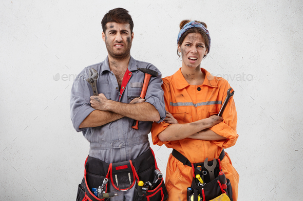 Professional female and male plumbers with untidy faces, look unhappily ...