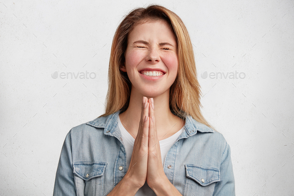 Beautiful pleased young female has broad smile, rouge cheeks, closes ...