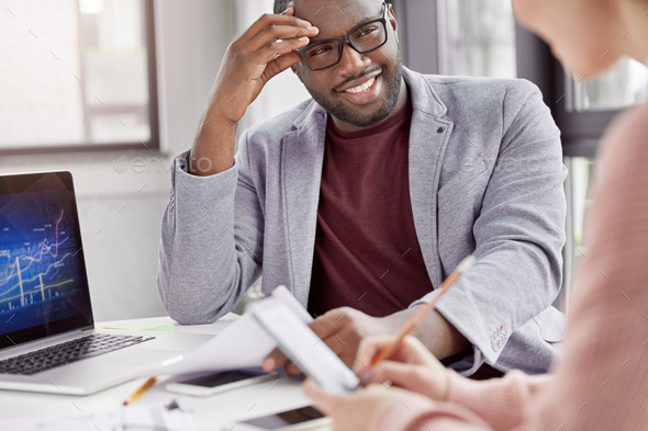 Cropped shot of cheerful dark skinned male boss and female secretary ...