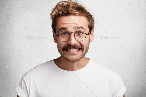 Funny attractive bearded young male with comic smile, has awkward look ...