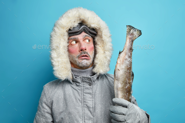 Indoor shot of thoughtful frozen unshaven man holds big trophy fish ...