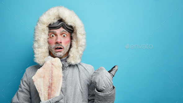 Embarrassed shocked man fisher holds frozen fish after winter ice ...