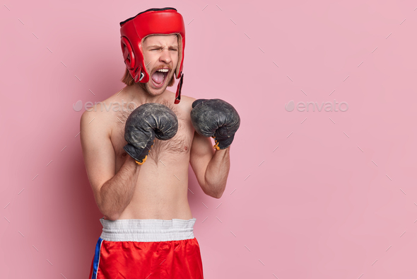 Horizontal shot of angry boxer screams loudly trains in gym prepares ...