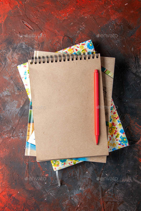 Vertical view of several stacked spiral notebooks with pen on dark ...