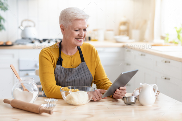 Cheerful aged lady cooking in kitchen, holding digital tablet Stock ...
