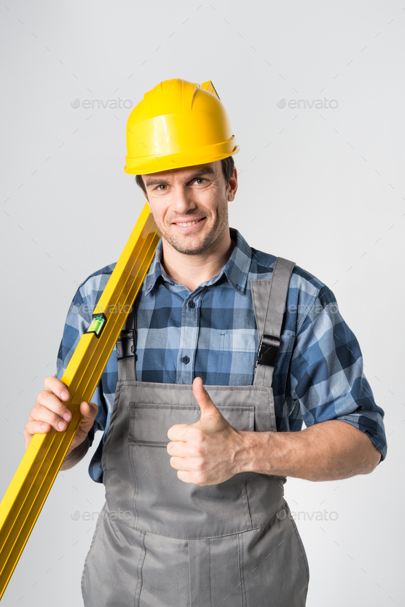 Smiling workman with level tool showing thumb up isolated on grey Stock ...