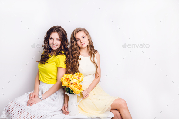 Studio photo of two smiling girls sitting shoulder to shoulder ...