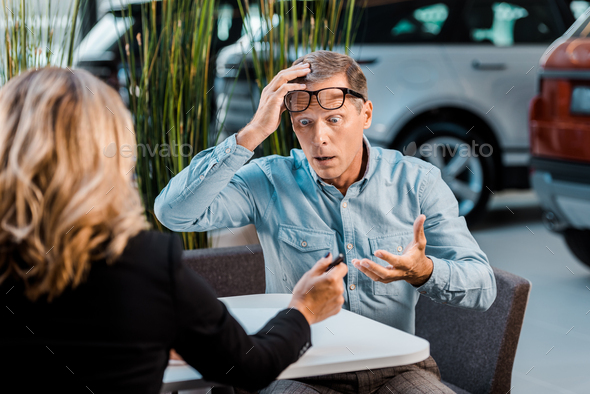 shocked adult customer and female car dealer sitting in showroom Stock ...