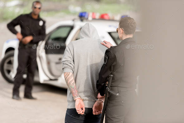 rear view of policewoman arresting male criminal in handcuffs while ...